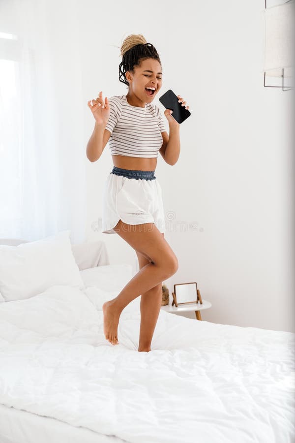 Young Black Woman Singing while Dancing with Cellphone on Bed Stock ...