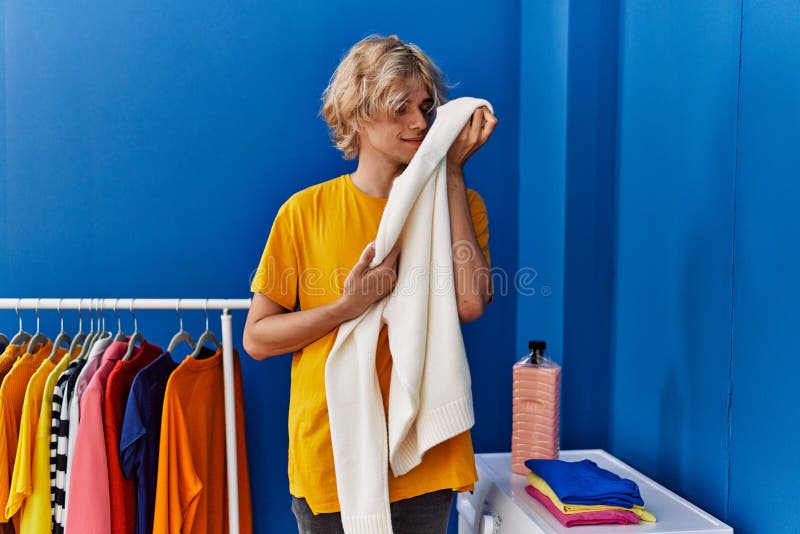 Young Blond Man Smiling Confident Smelling Clothes at Laundry Room ...