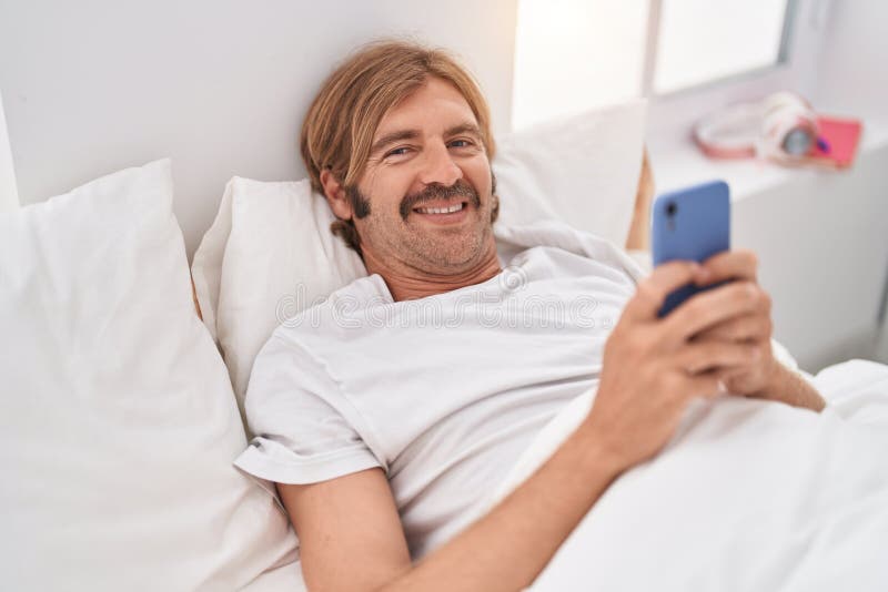 Young Blond Man Using Smartphone Lying on Bed at Bedroom Stock Photo ...