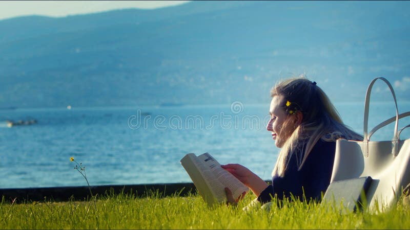 Young Blond Woman is Relax and Reading Book on Grass in Nature Stock ...