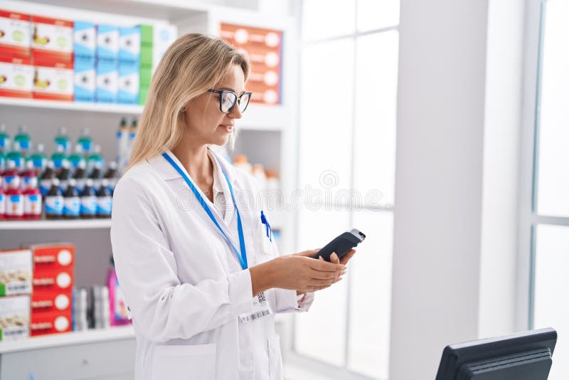 Young Blonde Woman Pharmacist Using Data Phone Working at Pharmacy ...