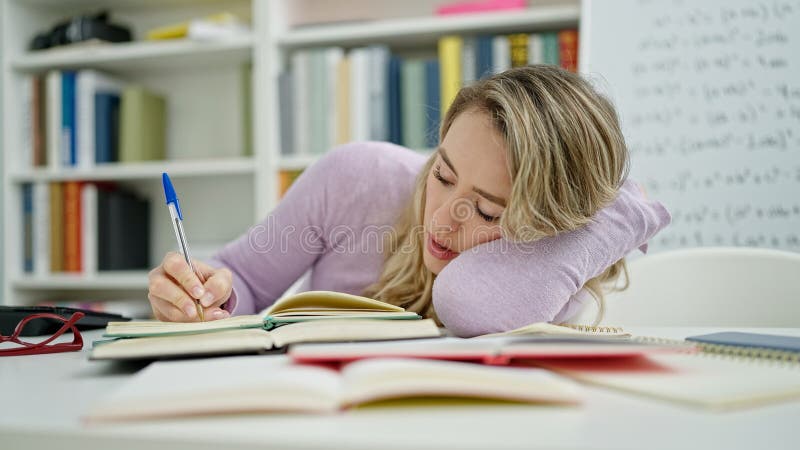 Young Blonde Woman Student Tired Writing Notes at Classroom Stock Photo ...