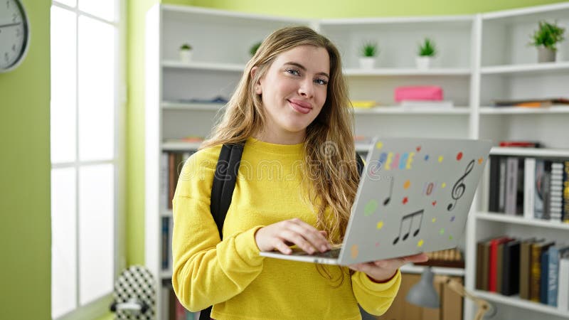 Young Blonde Woman Student Wearing Backpack Using Laptop at Library ...