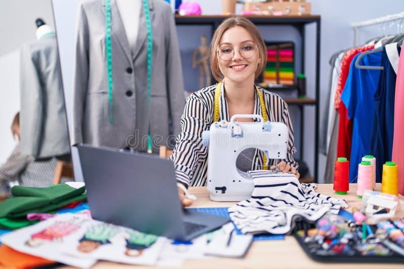 Young Blonde Woman Tailor Using Sewing Machine and Laptop at Tailor ...