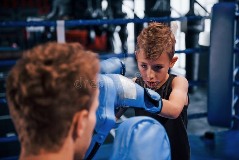 Young Boxing Coach is Helping Little Boy in Protective Wear on the Ring ...