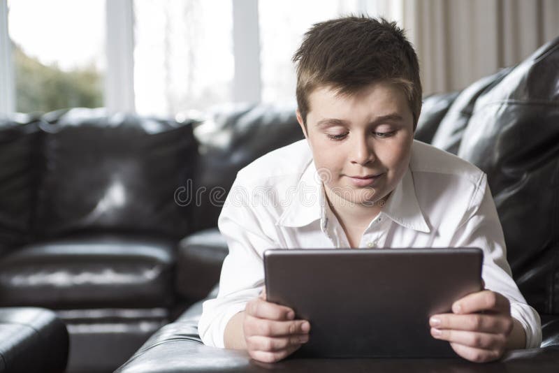 Young Boy Child Resting on His Hands Laying Down a Sofa Using Tablet ...