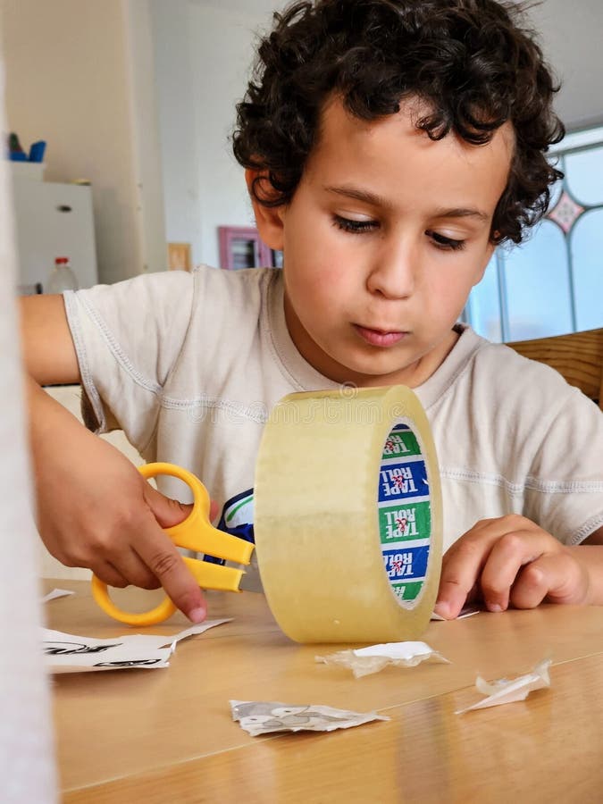 Young Boy Cutting a Piece of Tape with Scissors at the Table. Stock ...