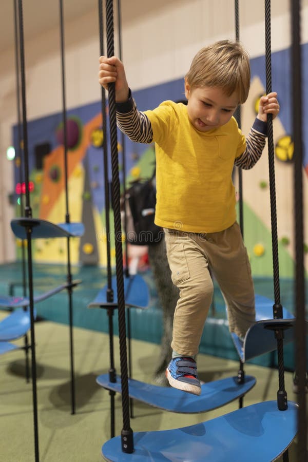 A Young Boy is Hanging from a Rope and Balancing on a Blue Platform ...