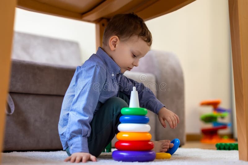 Young Boy Playing with Colorful Stacking Rings Under Table, Focused on ...