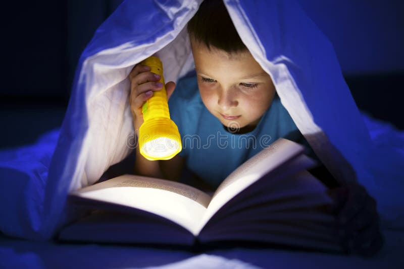 A Young Boy Reading a Book Under the Covers with a Flashlight at Dark ...