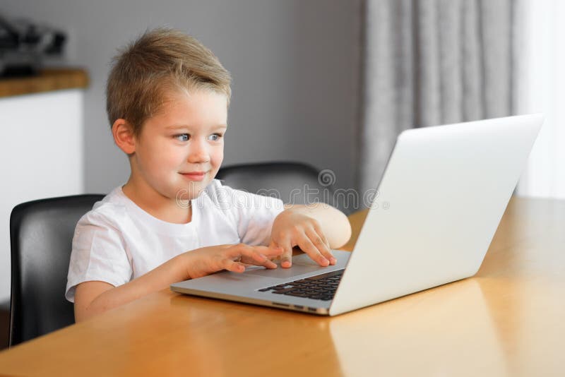A Young Boy Using a Laptop Computer Sitting on Top of a Table at Home ...