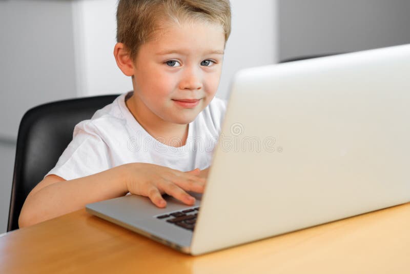 A Young Boy Using a Laptop Computer Sitting on Top of a Table at Home ...