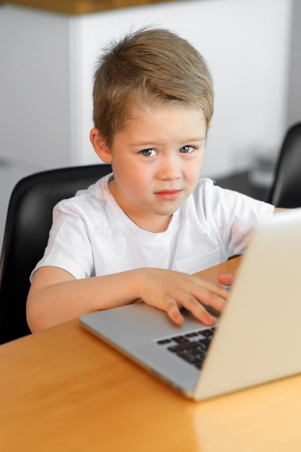 A Young Boy Using a Laptop Computer Sitting on Top of a Table at Home ... A Young Boy Using a Laptop Computer Sitting on Top of a Table at Home ...