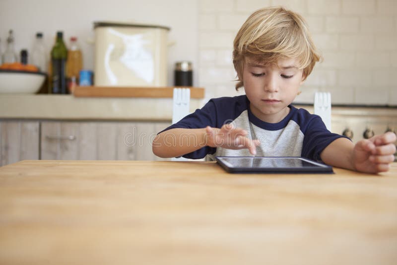 Young Boy Using Tablet Computer at Kitchen Table, Front View Stock ...