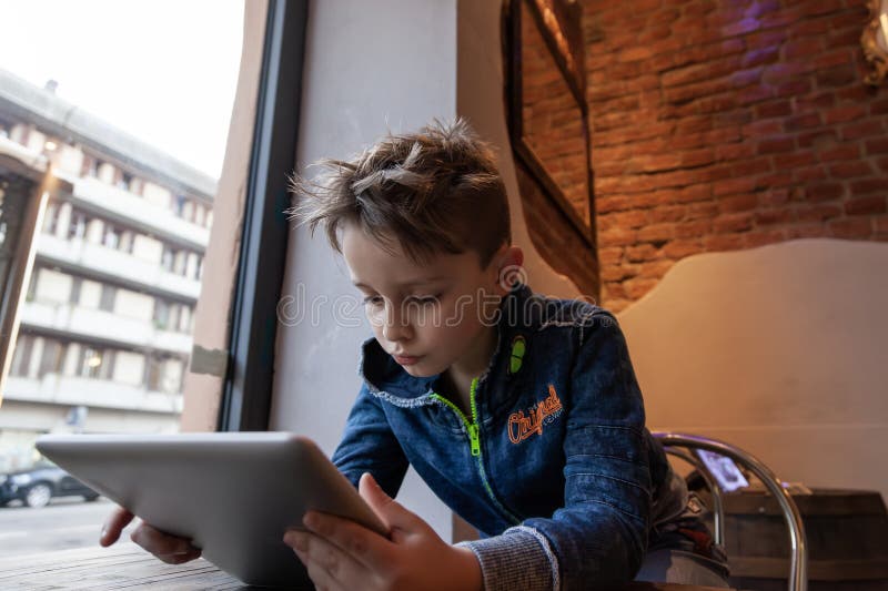 Young Boy Using a Tablet Sitting in a Pub in Front of a Large Window ...
