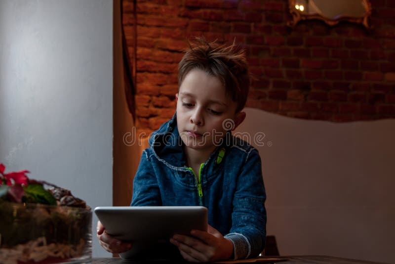 Young Boy Using a Tablet Sitting in a Pub in Front of a Large Window ...