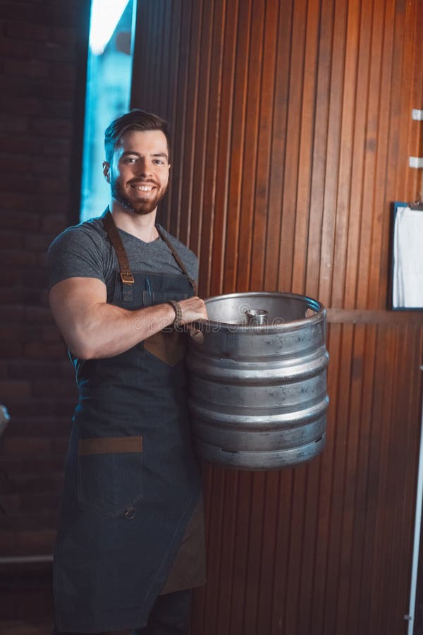 A Young Brewer in an Apron Holds a Barrel with Beer in the Hands Stock ...