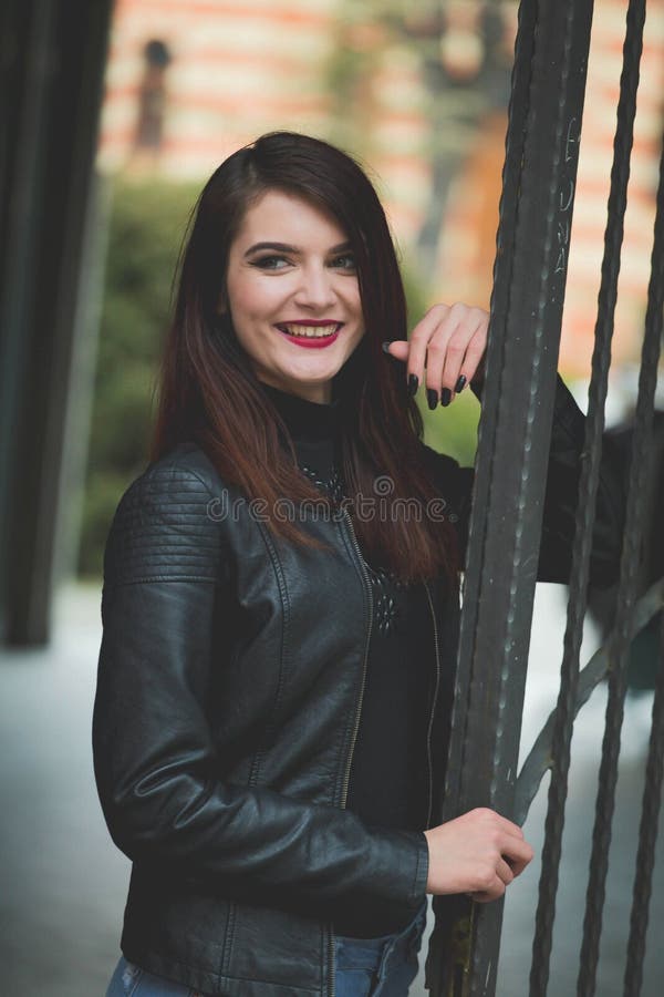 Young Brunette Female in a Leather Jacket Posing in Front of a Gate ...