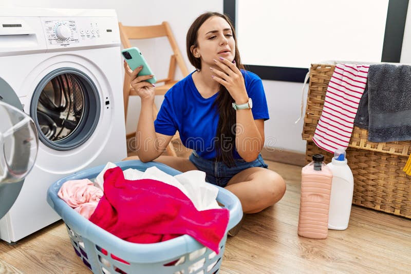 Young Brunette Woman Doing Laundry Using Smartphone with Hand on Chin ...
