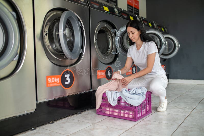 Young Brunette Woman Sorting Clothes in Laundromat in the Laundry ...