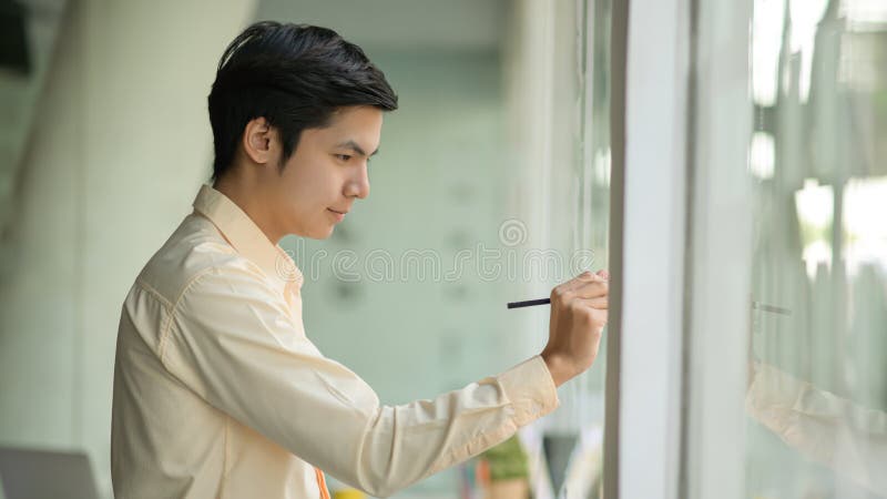 Young Business Man is Taking Notes Working on a Note on a Glass Wall in ...