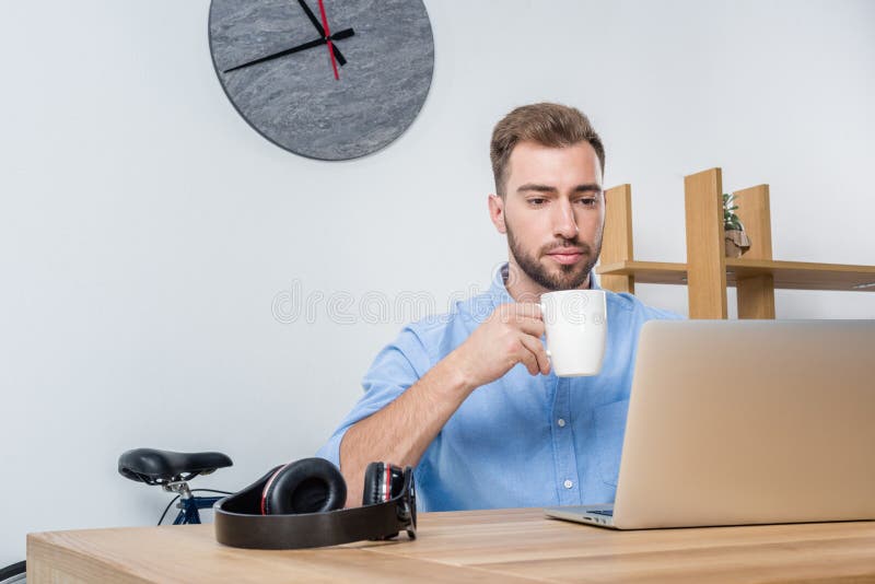 Young Businessman Drinking Coffee while Working with Laptop in Office ...