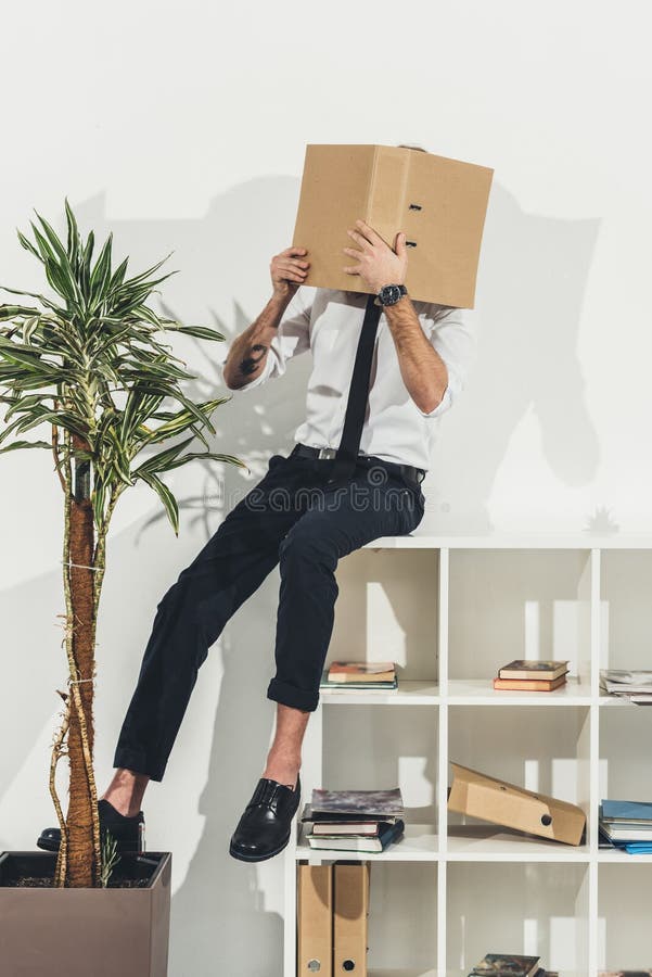 Young Businessman Hiding Face with Folder while Sitting on Bookshelf ...