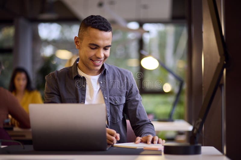 Young Businessman Working on Laptop at Desk in Office Making Notes ...