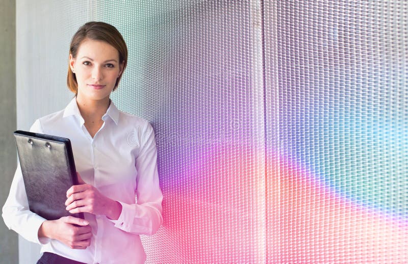 Young Businesswoman Standing while Holding File in Office with Lens ... Young Businesswoman Standing while Holding File in Office with Lens ...