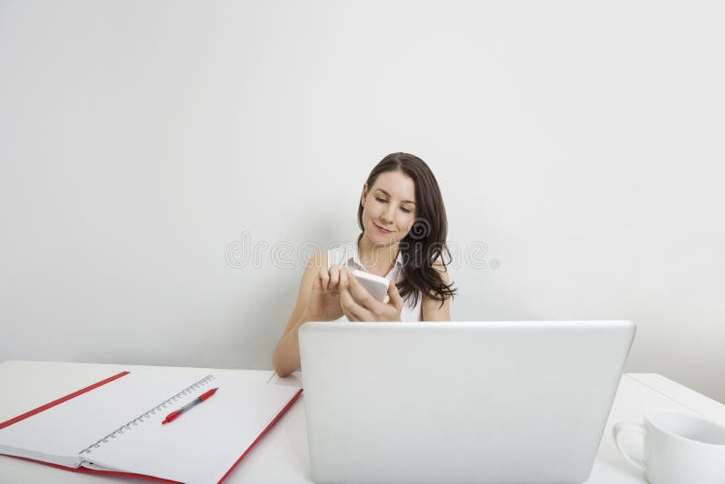 Young Businesswoman Using Cell Phone at Desk in Office Stock Photo ...