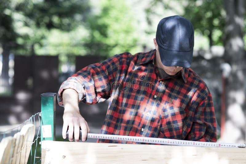 Young Carpenter Measuring Wood Using a Tape Measure in the Garden Stock ...