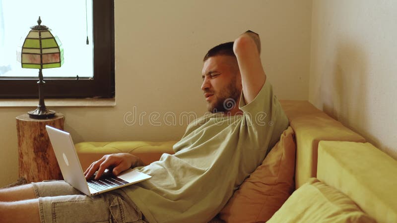 A Young Caucasian Bearded Man is Sitting at Home Working Using a Laptop ...