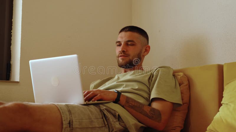 A Young Caucasian Bearded Man is Sitting at Home Working Using a Laptop ...