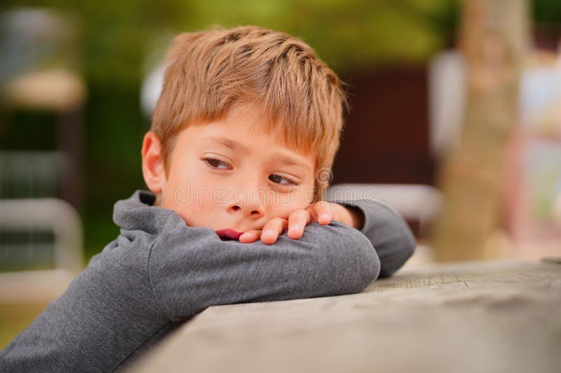 Young Caucasian Boy Sits on a Bench, Resting His Head on His Arm in a ...