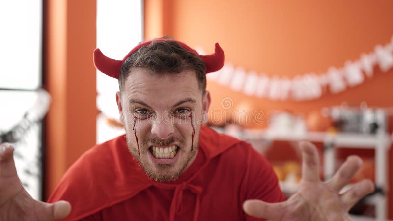 Young Caucasian Man Screaming Wearing Devil Costume Sitting on the Sofa ...