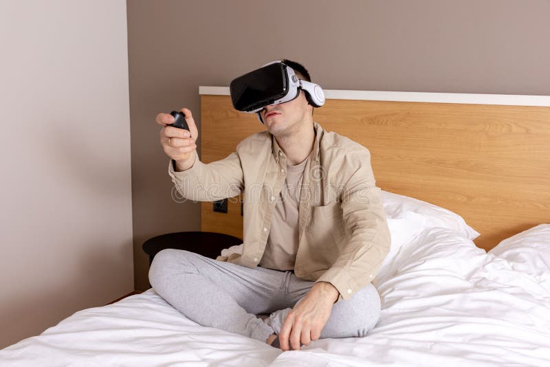 Young Caucasian Man Sitting on Bed at Home with VR Headset and Playing ...