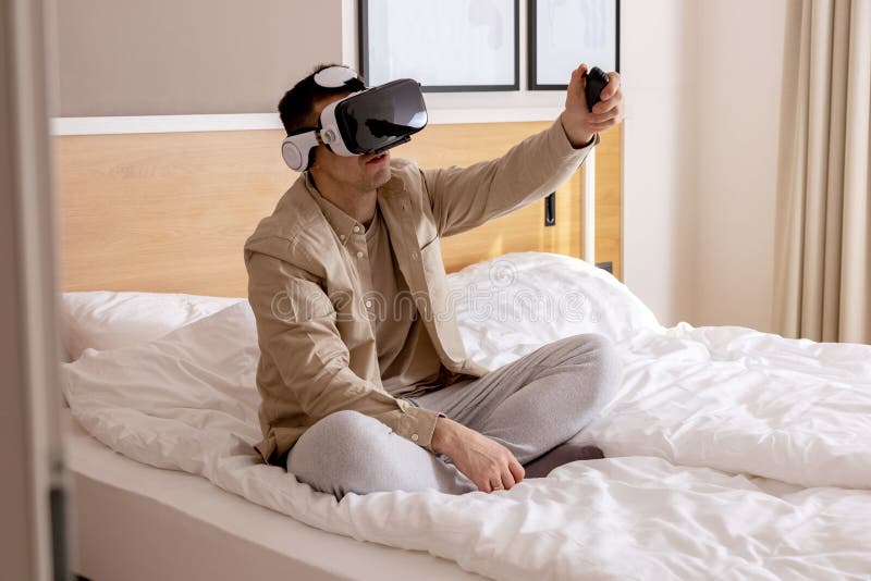 Young Caucasian Man Sitting on Bed at Home with VR Headset and Playing ...