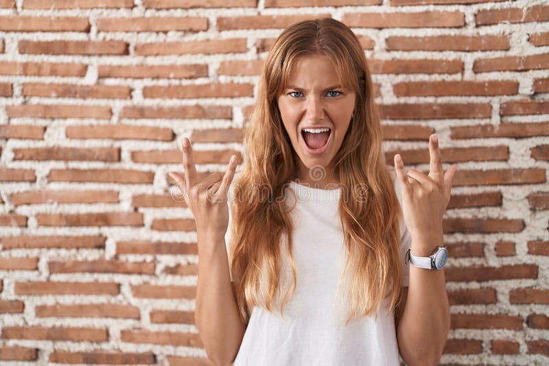 Young Caucasian Woman Standing Over Bricks Wall Shouting With Crazy