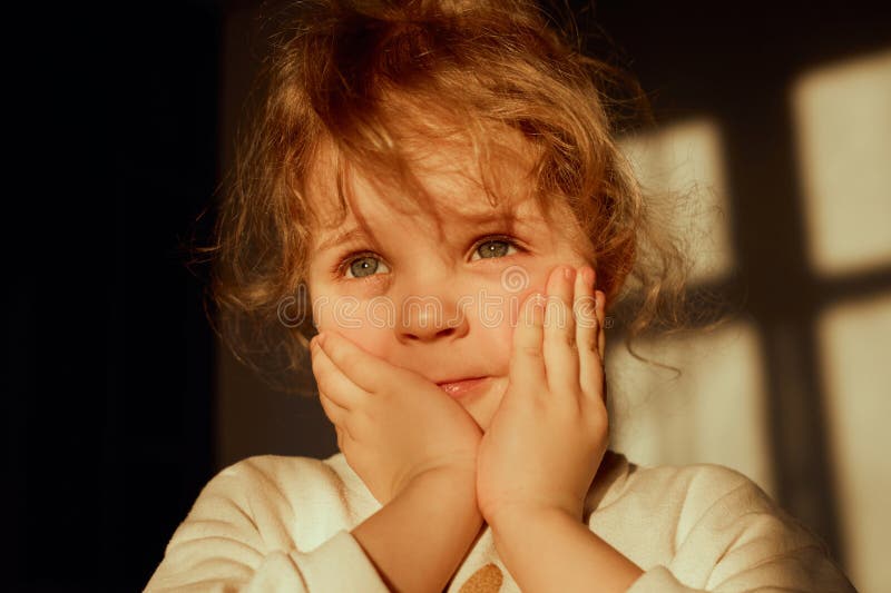 A Young Child with Curly Hair Displays a Pensive Expression while ...