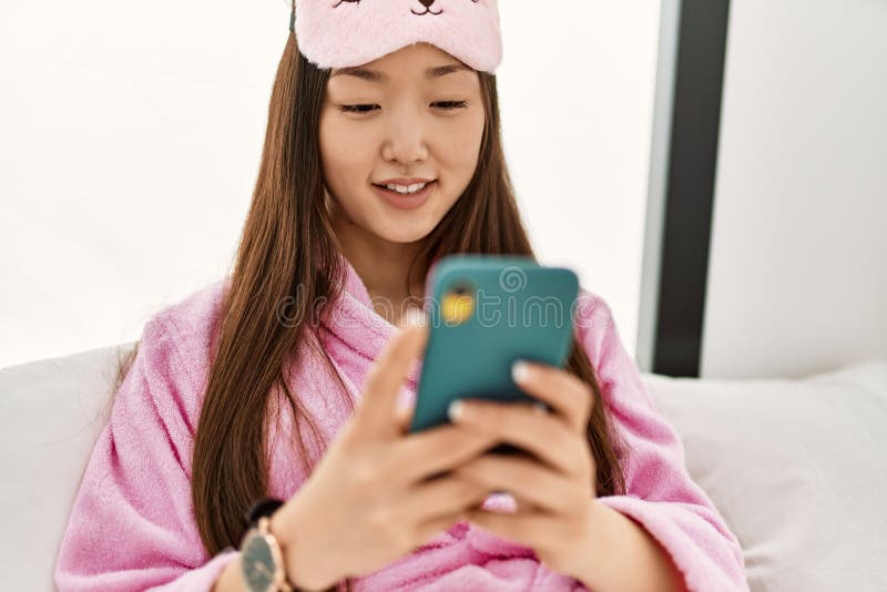 Young Chinese Girl Using Smartphone Lying On The Bed At Bedroom Stock