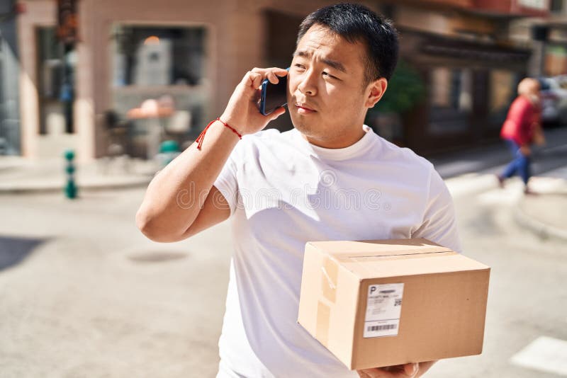 Young Chinese Man Courier Talking on the Smartphone Holding Package at ...