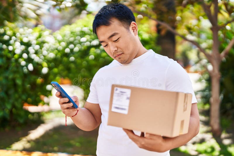Young Chinese Man Courier Using Smartphone Holding Package at Park ...