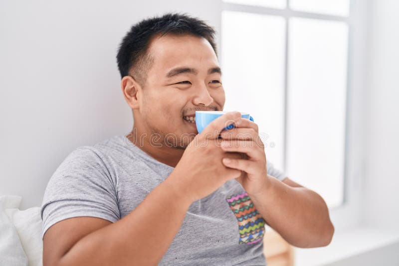 Young Chinese Man Drinking Cup of Coffee Sitting on Bed at Bedroom ...