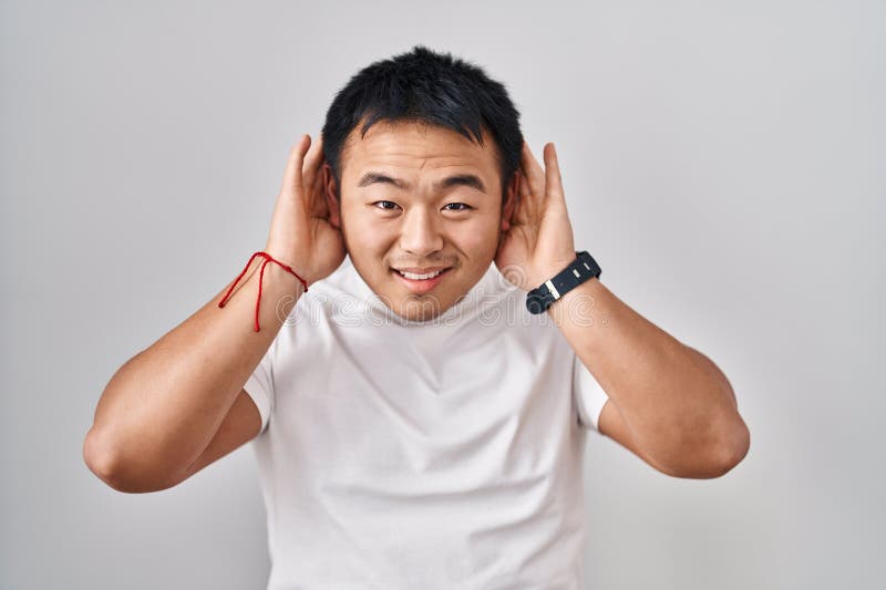 Young Chinese Man Standing Over White Background Trying To Hear Both ... Young Chinese Man Standing Over White Background Trying To Hear Both ...