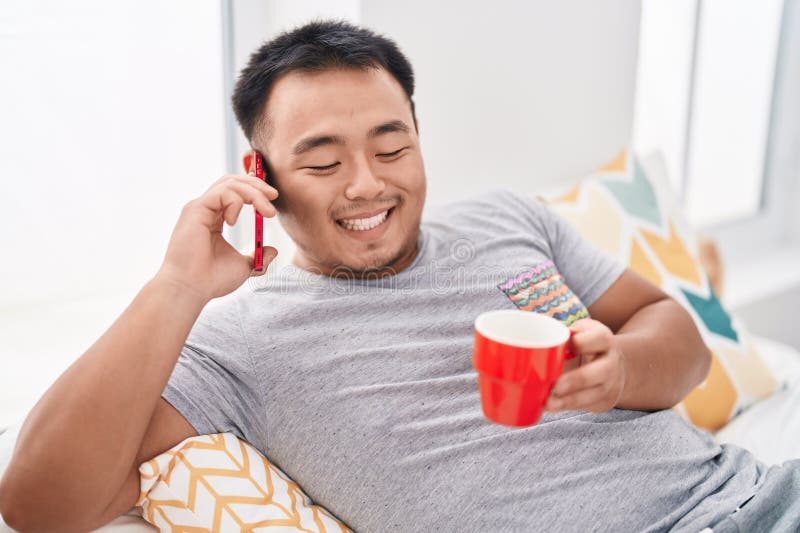 Young Chinese Man Talking on Smartphone Drinking Coffee at Bedroom ...