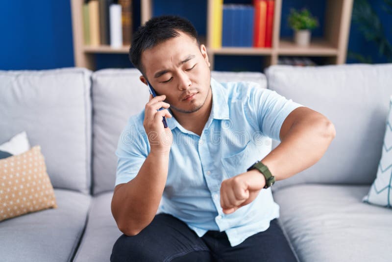 Young Chinese Man Talking on the Smartphone Looking Watch at Home Stock ...