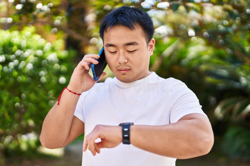 Young Chinese Man Talking on the Smartphone Looking Watch at Park Stock ...