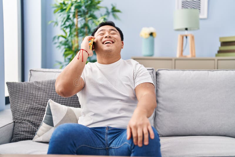 Young Chinese Man Talking on the Smartphone Sitting on Sofa at Home ...