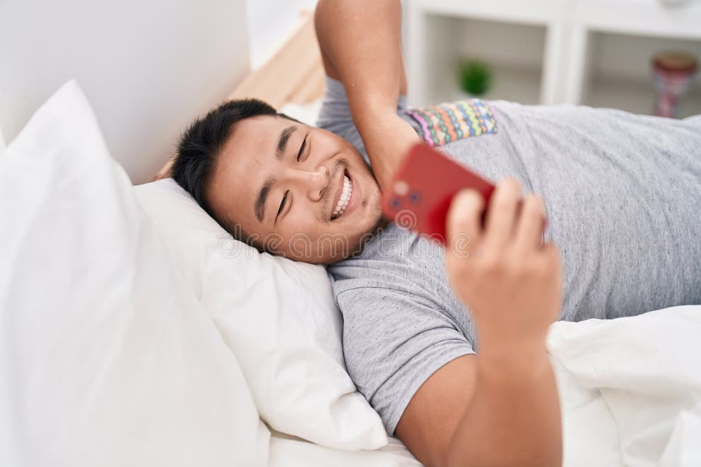 Young Chinese Man Using Smartphone Lying on Bed at Bedroom Stock Image ...