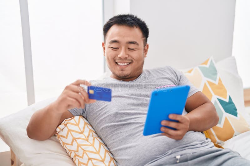 Young Chinese Man Using Touchpad and Credit Card Sitting on Bed at ...